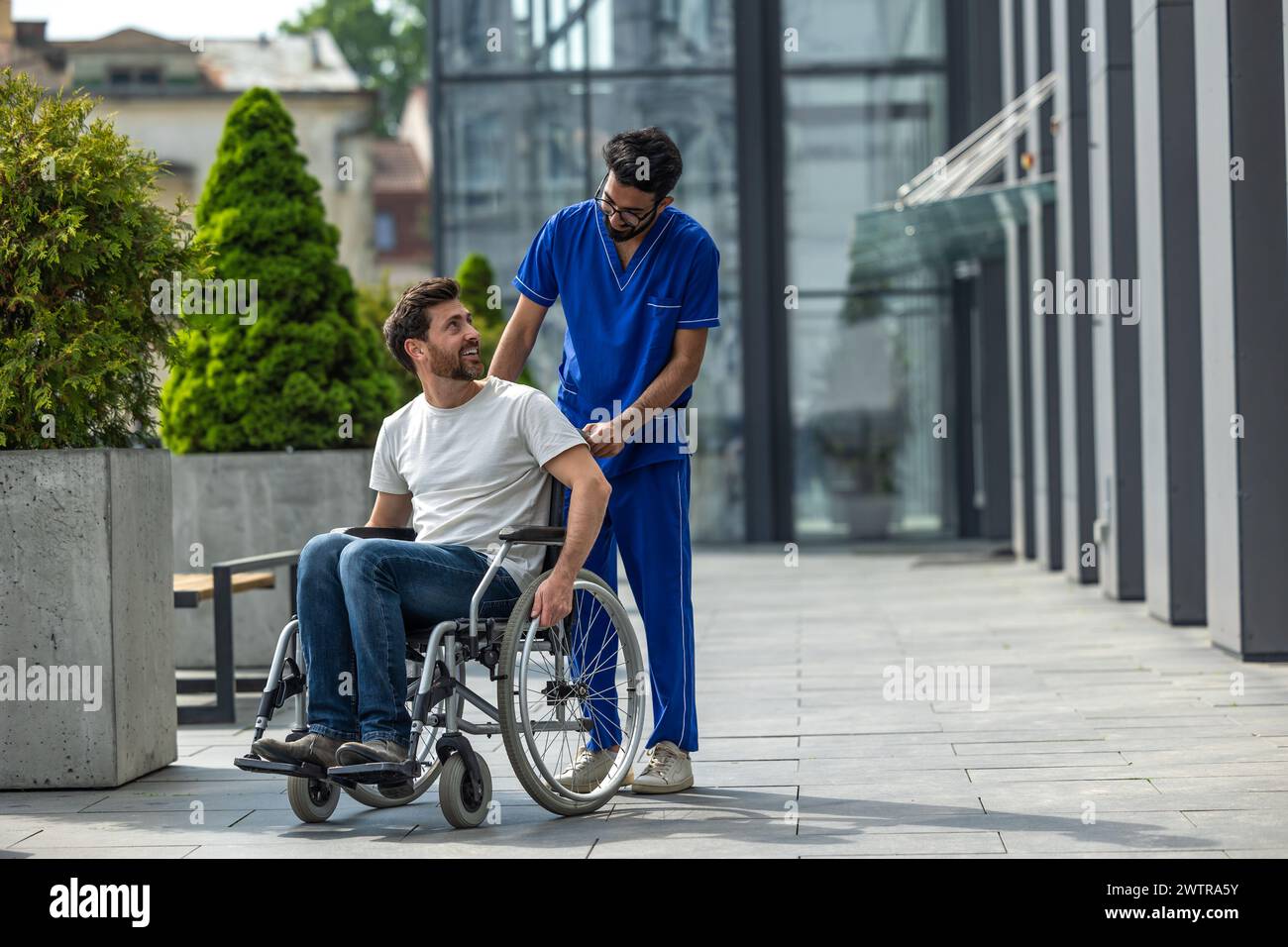 Brunette male nurse rolling a wheelchair with a patient Stock Photo - Alamy