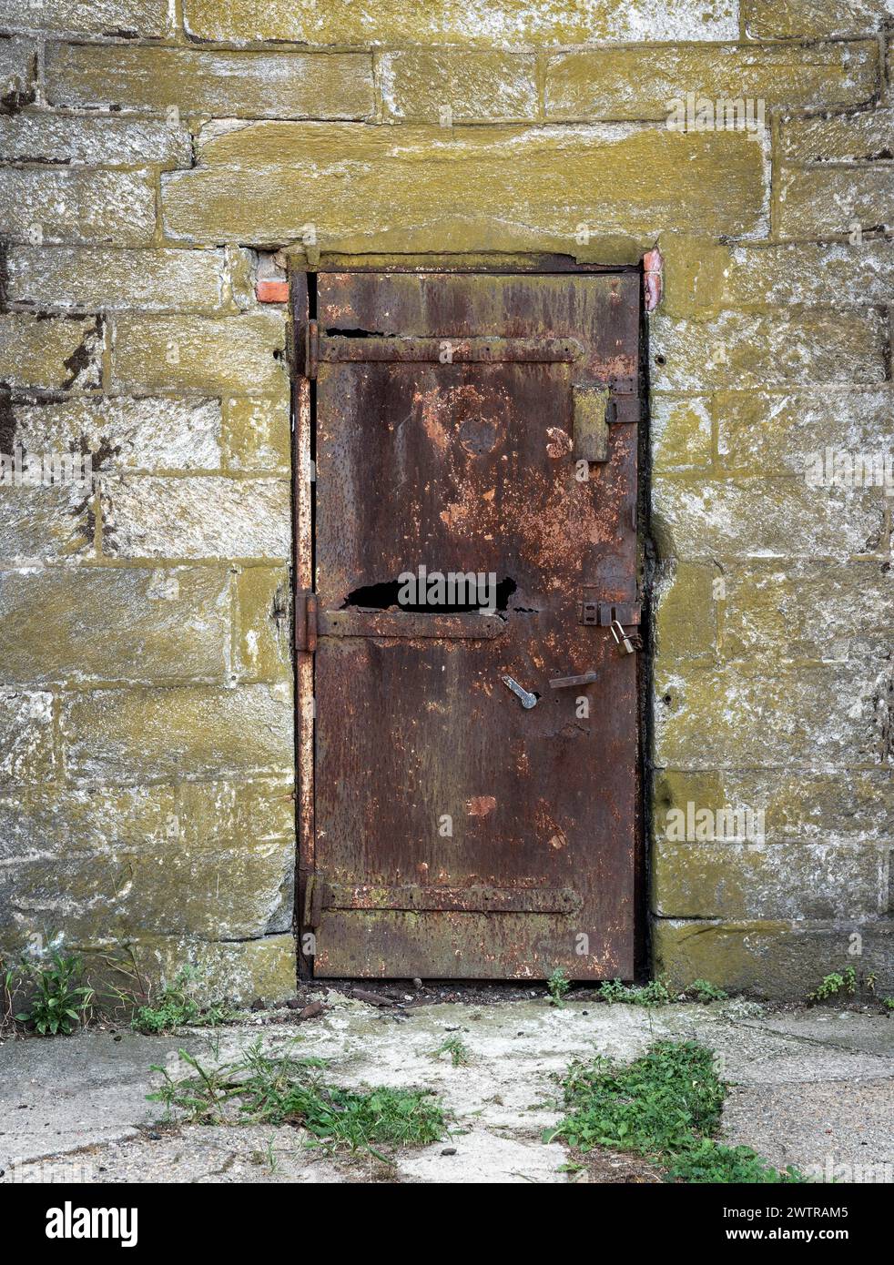 An old rusty iron door that is rusting through set in a stone wall ...