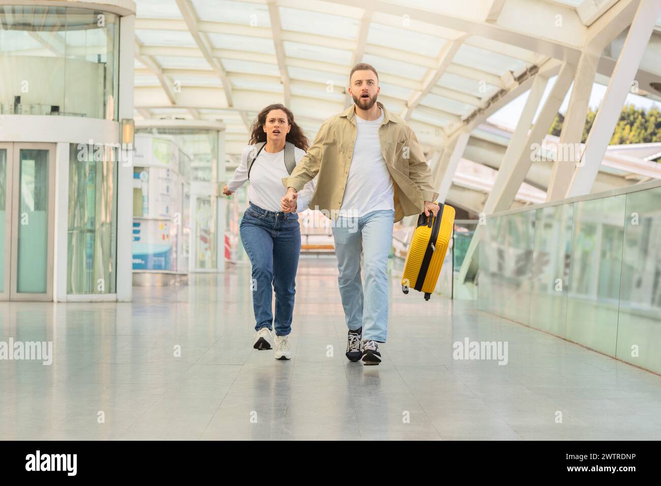 Determined couple sprinting through airport corridor with suitcase ...