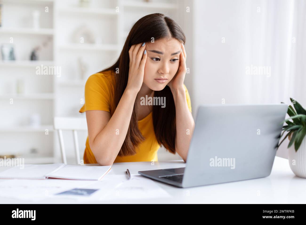 Anxious asian woman touching her head while looking at laptop screen ...