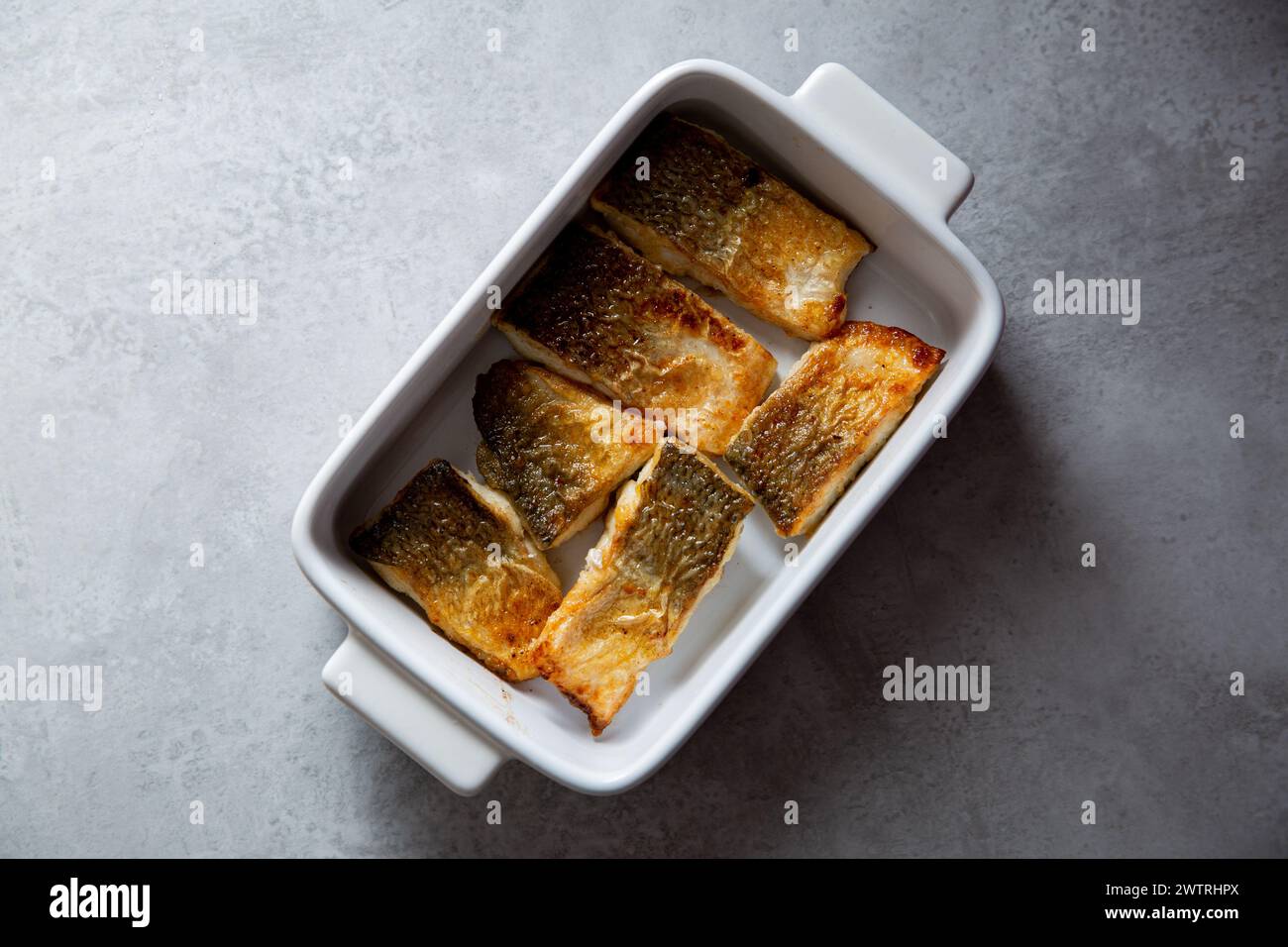 Baking dish with roasted whitefish fillet on kitchen counter. Hand ...