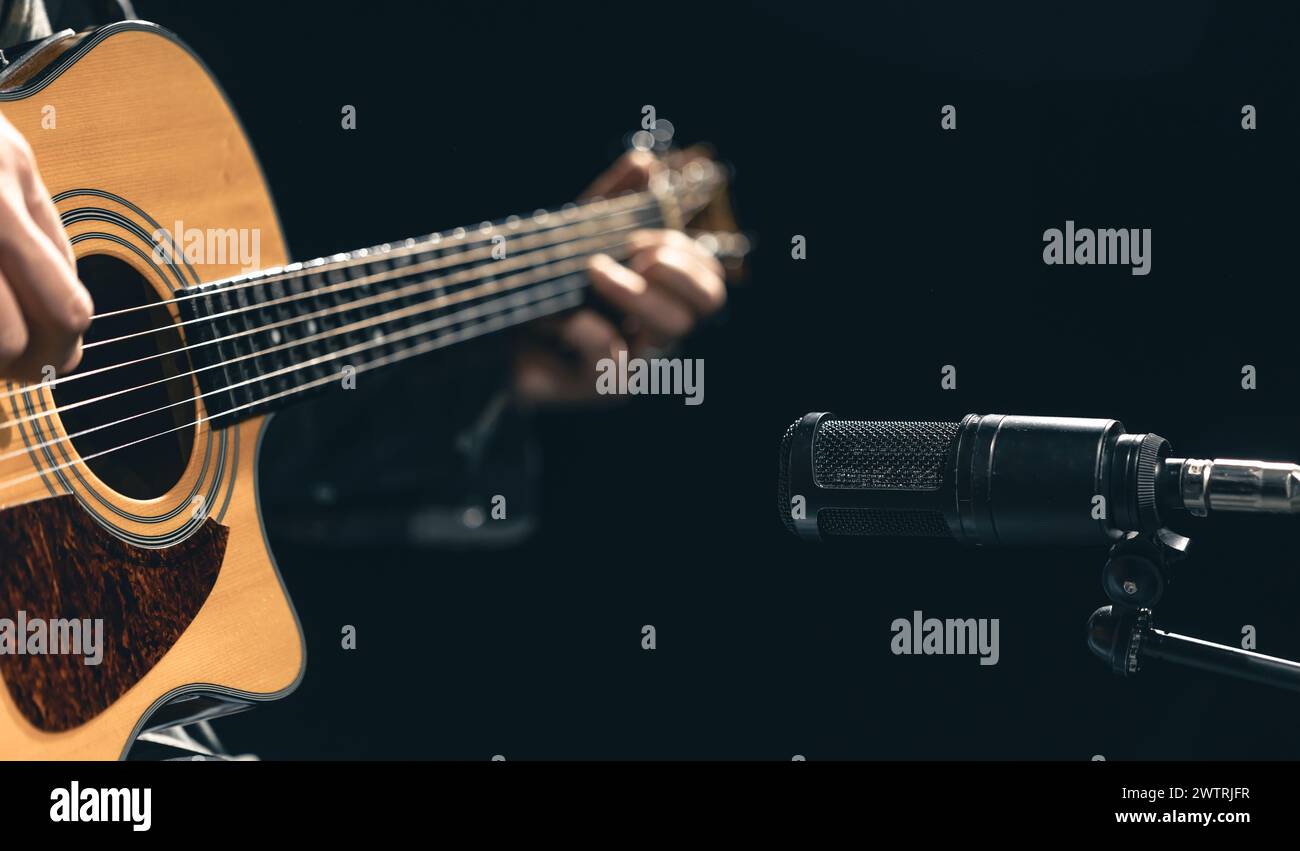 Male musician playing acoustic guitar behind microphone in recording ...
