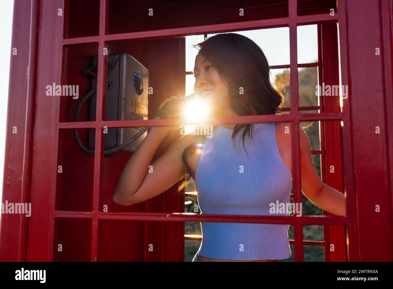 An attractive Asian woman in casual clothes is talking on an old phone ...