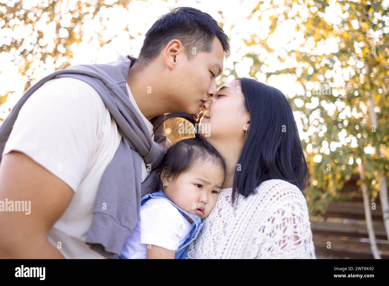 An Asian couple in love is kissing outdoors and holding their kid. Cute ...