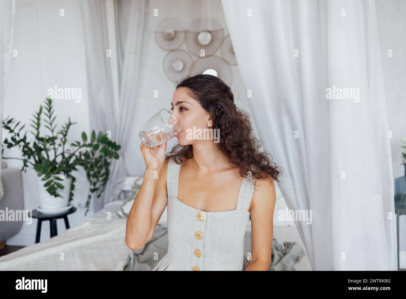A charming curly-haired brunette in a linen sundress holds a ...