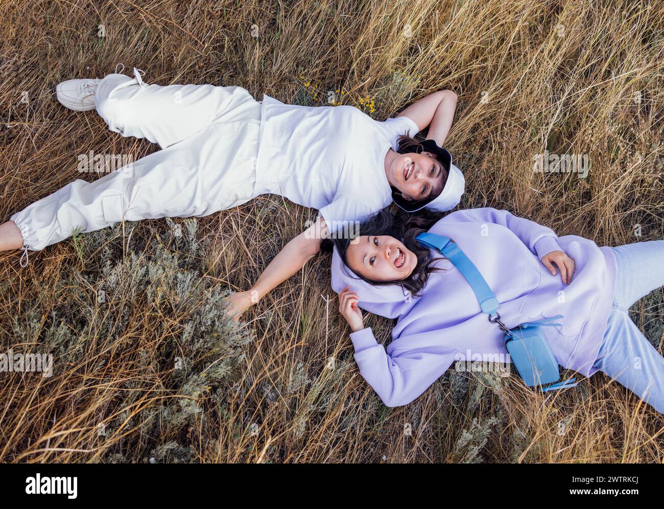 Two multiethnic friends are lying on the dry grass and laughing. Young ...