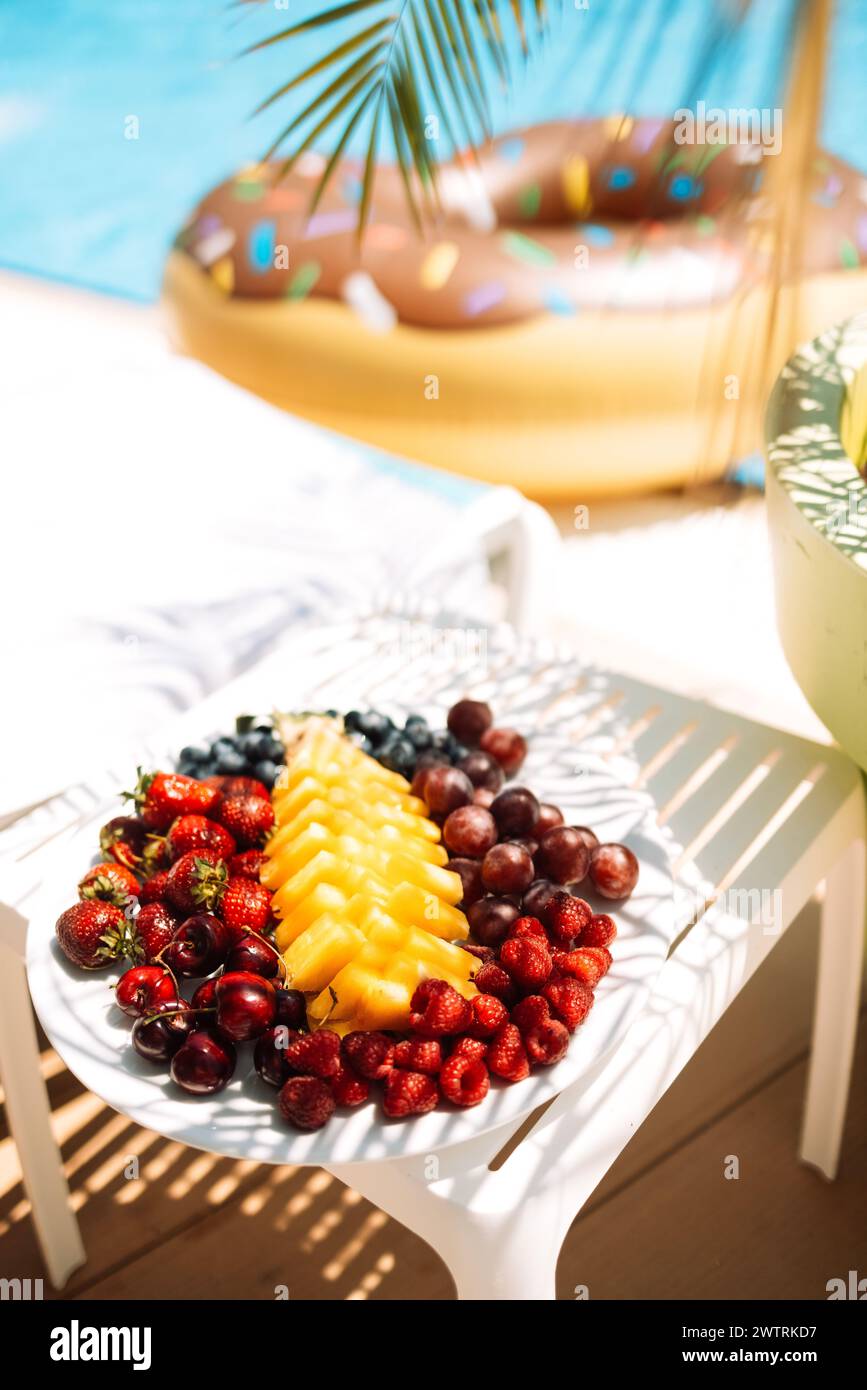 Delicious juicy fruit and berry set on the table by the pool. Pineapple ...