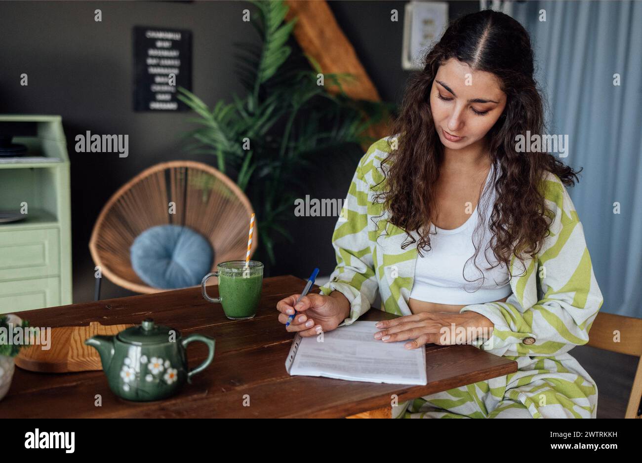 Charming curly-haired brunette in casual clothes signs documents at ...