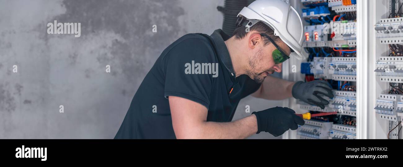 A male electrician works in a switchboard using an electrical ...