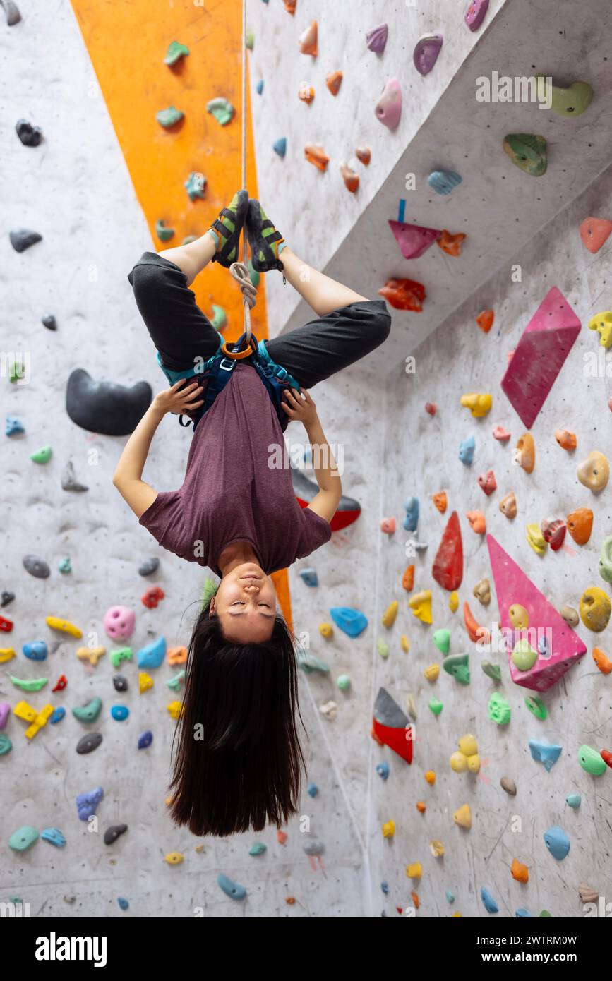 Young Asian woman on climbing wall. Korean funny girl is hanging upside ...