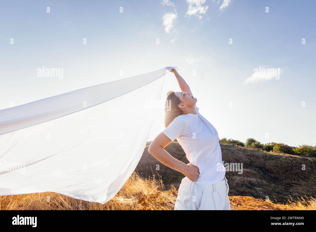 An attractive young woman smiles and holds an open white sheet outdoors ...