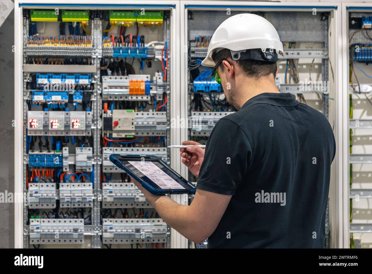 Man, an electrical working in a switchboard with fuses, uses a tablet Stock Photo - Alamy
