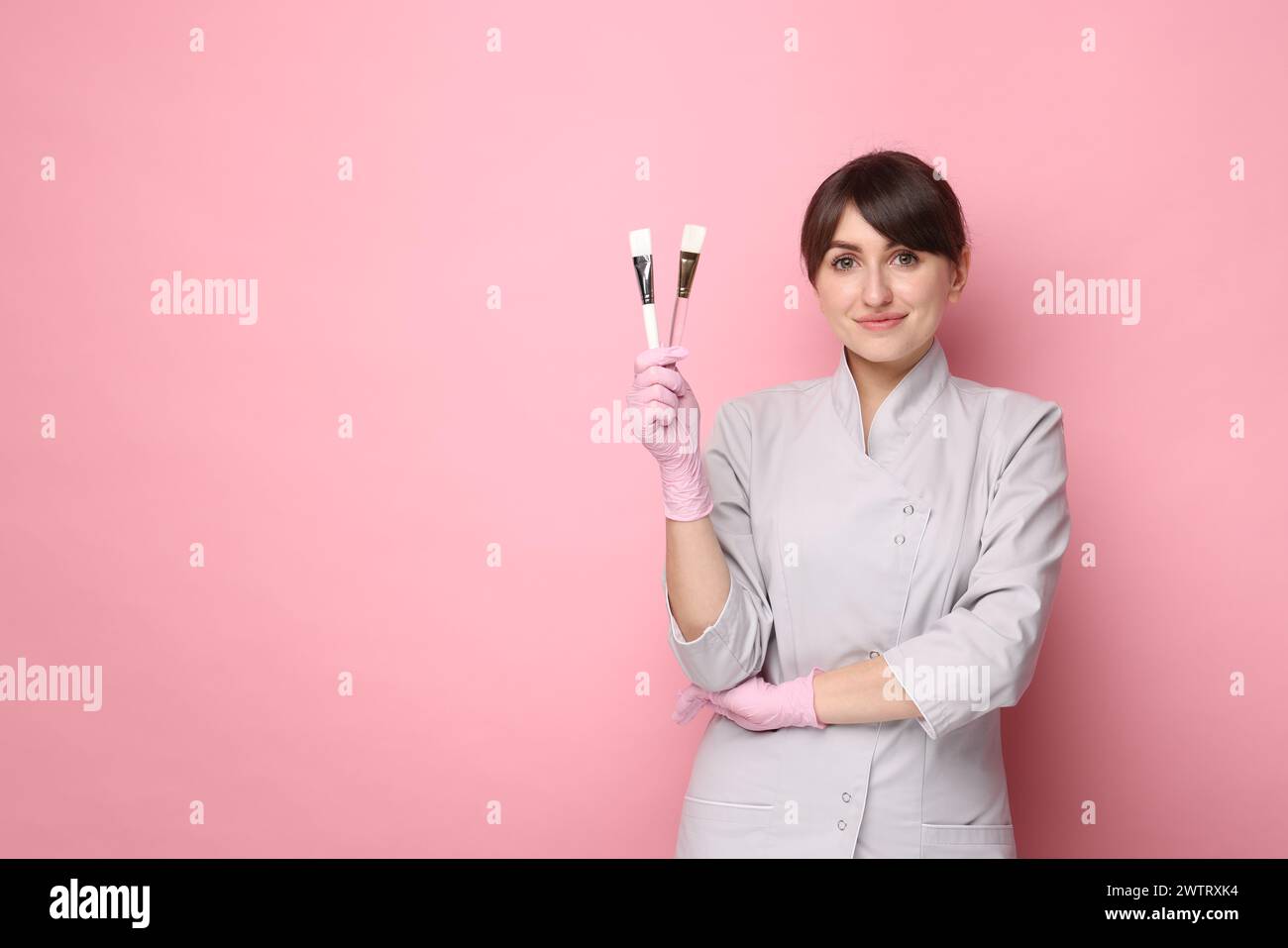 Cosmetologist with cosmetic brushes on pink background, space for text ...