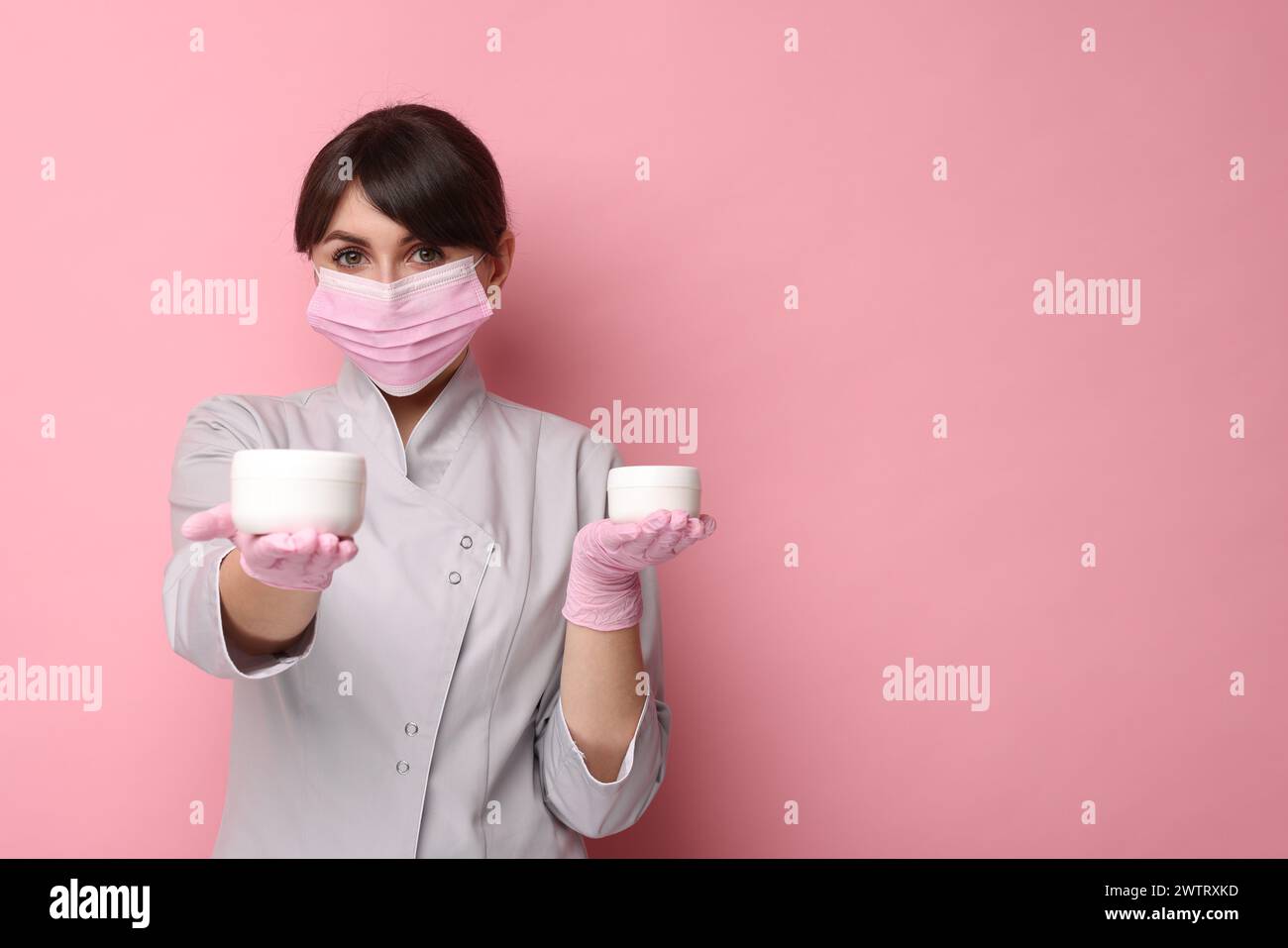 Cosmetologist with cosmetic products on pink background, space for text ...