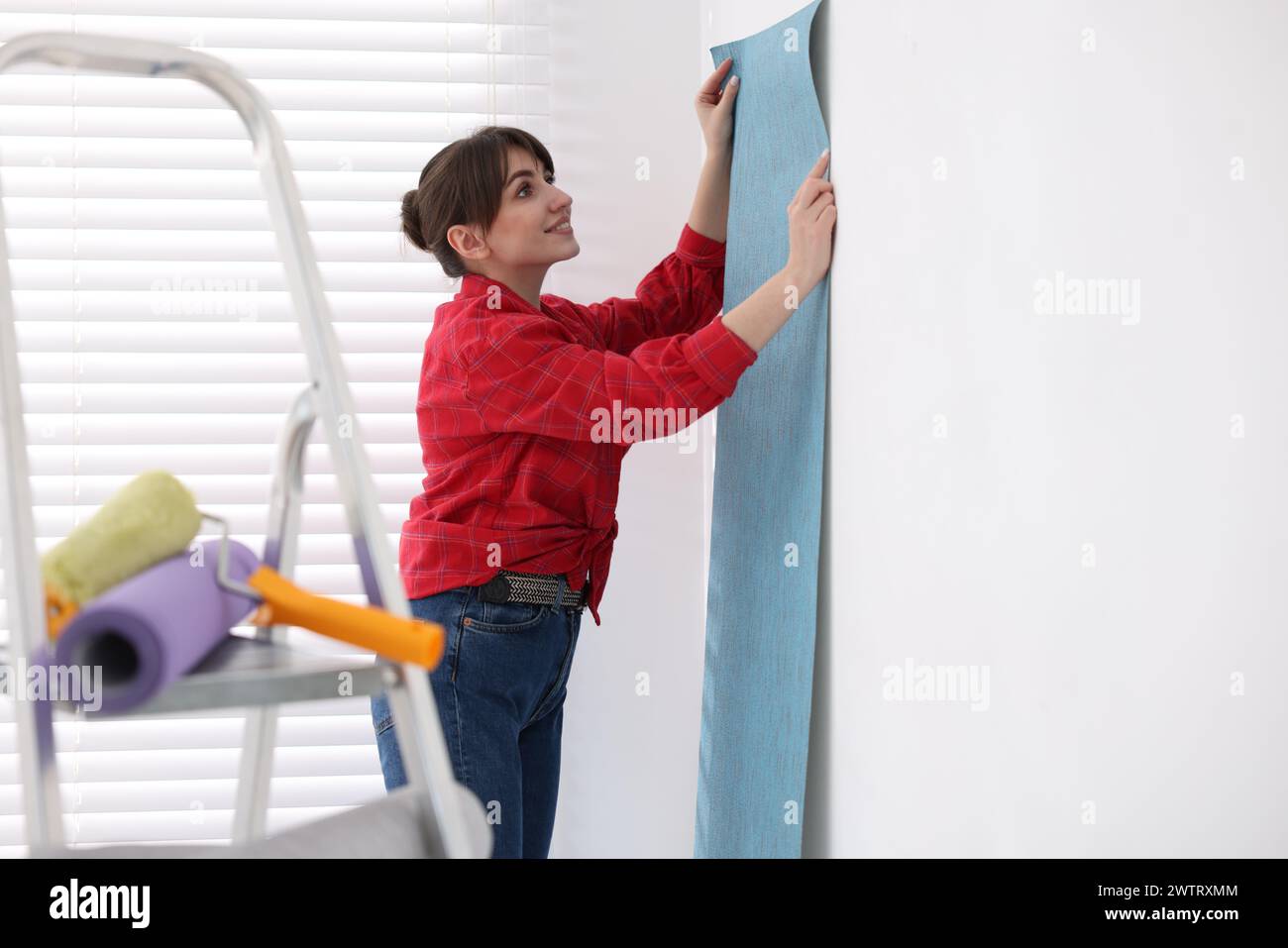 Woman hanging light blue wallpaper in room Stock Photo - Alamy