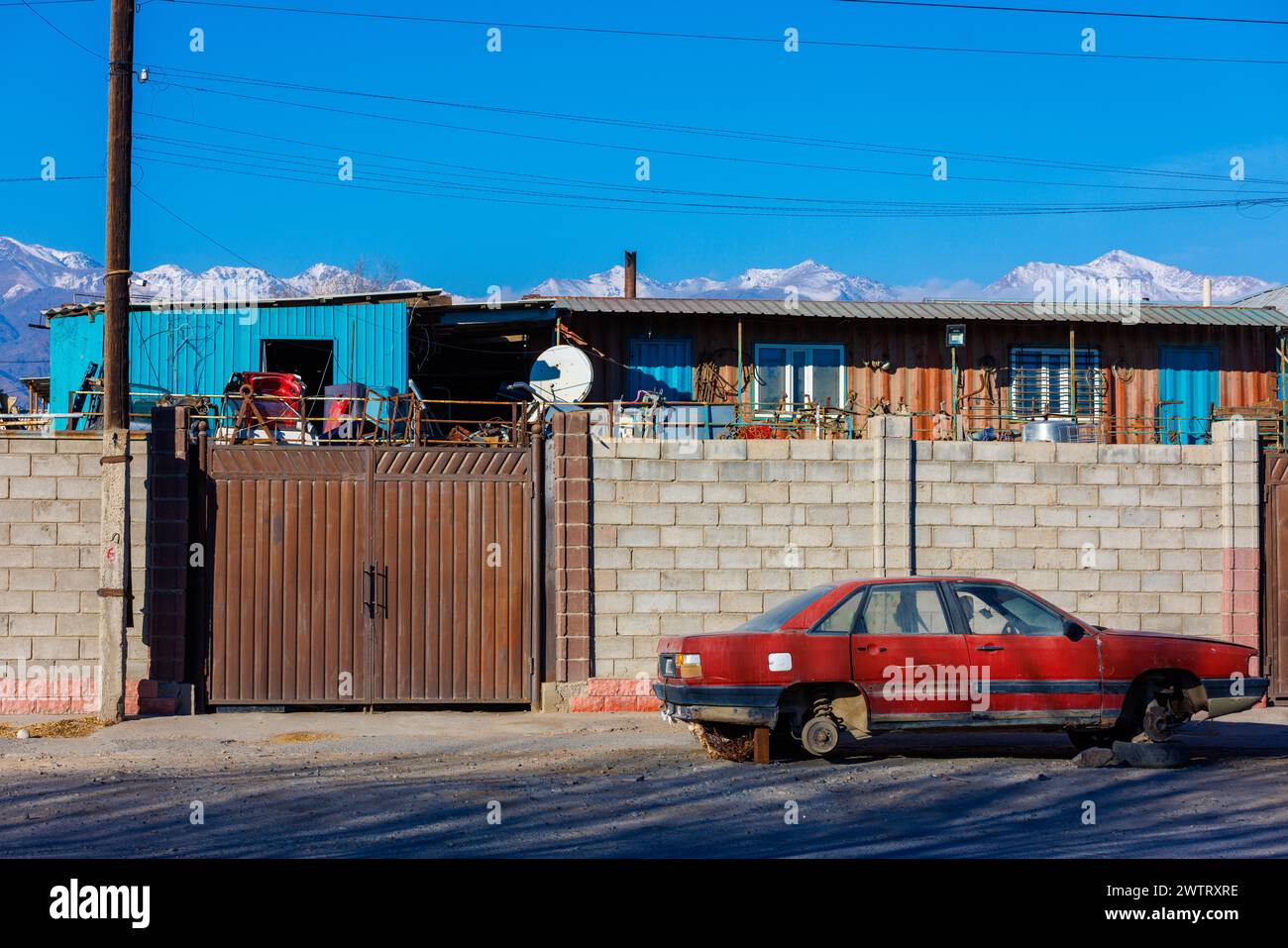 Red junked car without wheels in front of brick fence of junkyard ...