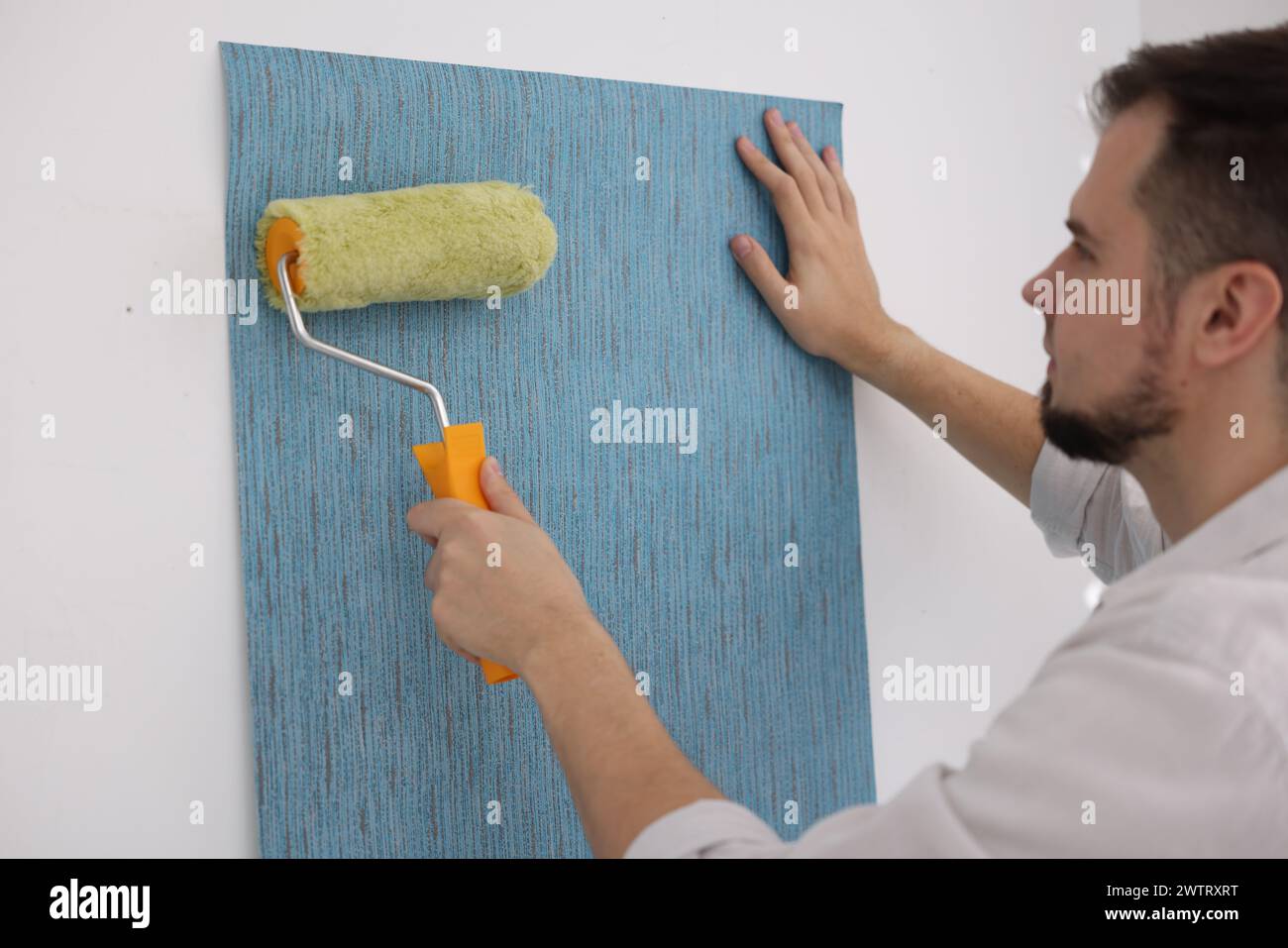 Man hanging light blue wallpaper in room Stock Photo - Alamy