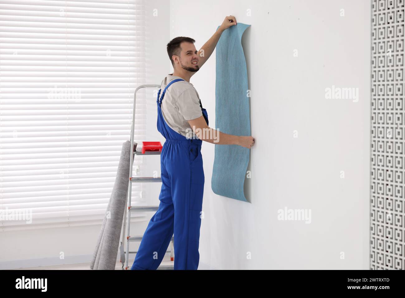Man hanging light blue wallpaper in room Stock Photo - Alamy