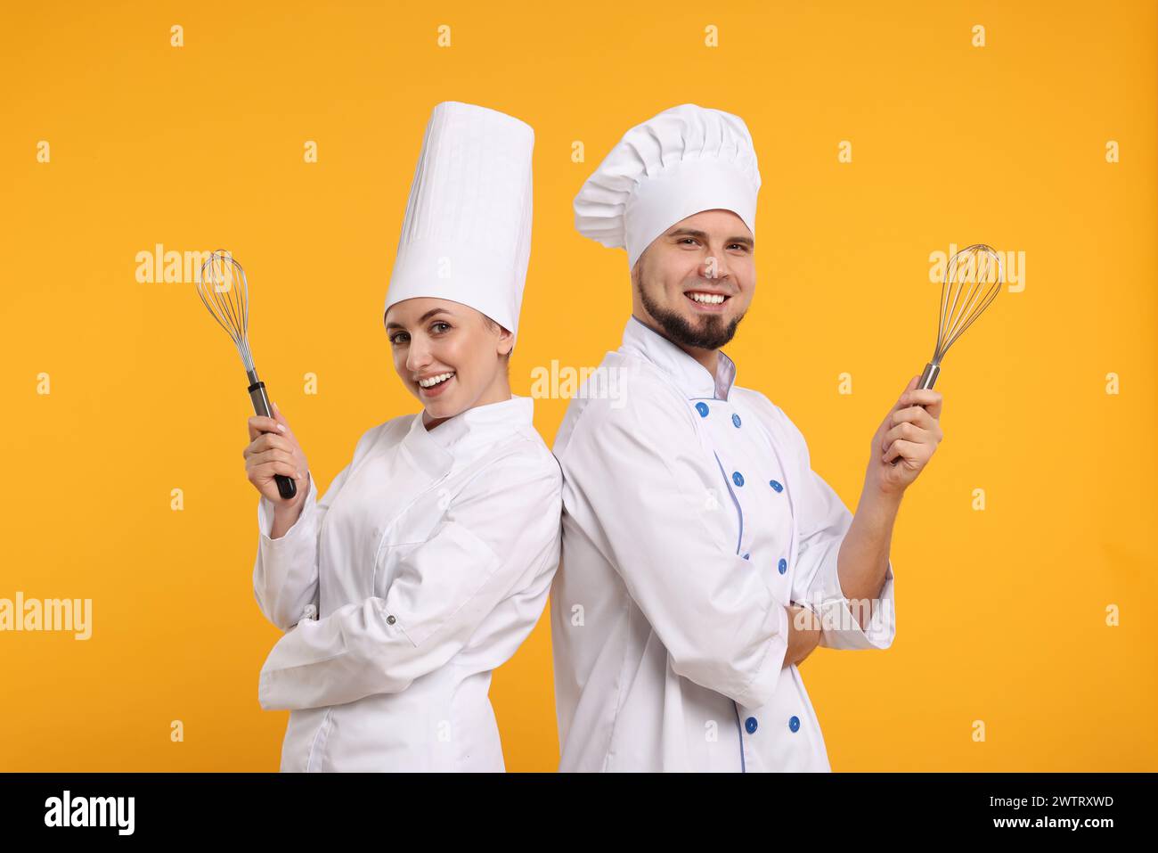 Happy professional confectioners in uniforms holding whisks on yellow ...
