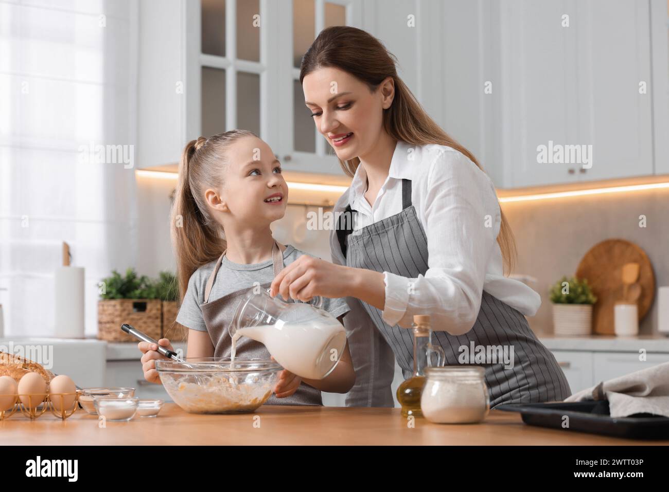 Making bread. Mother and her daughter pouring milk into bowl at wooden ...
