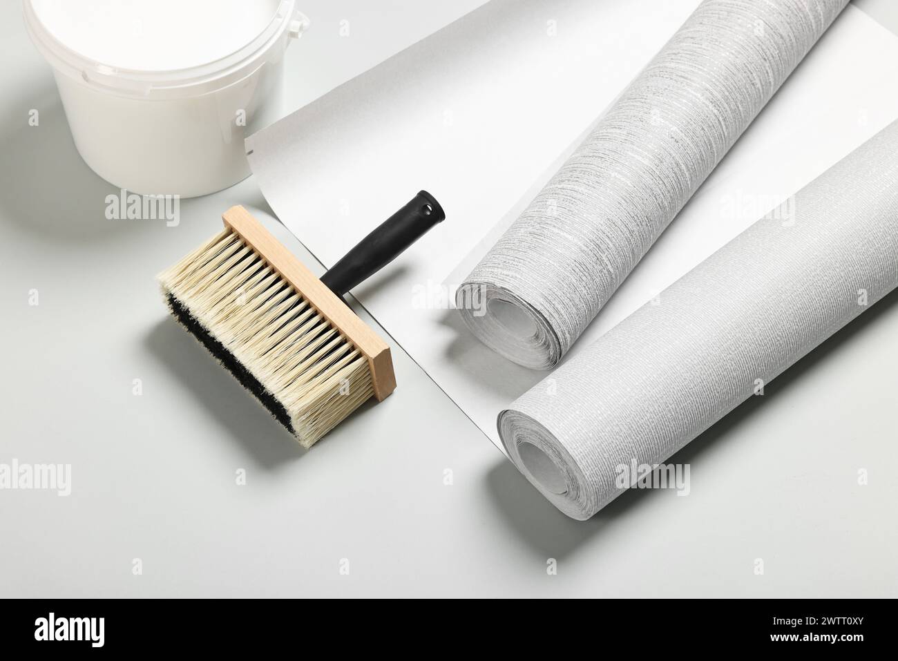Different wallpaper rolls, brush and bucket with glue on light grey ...