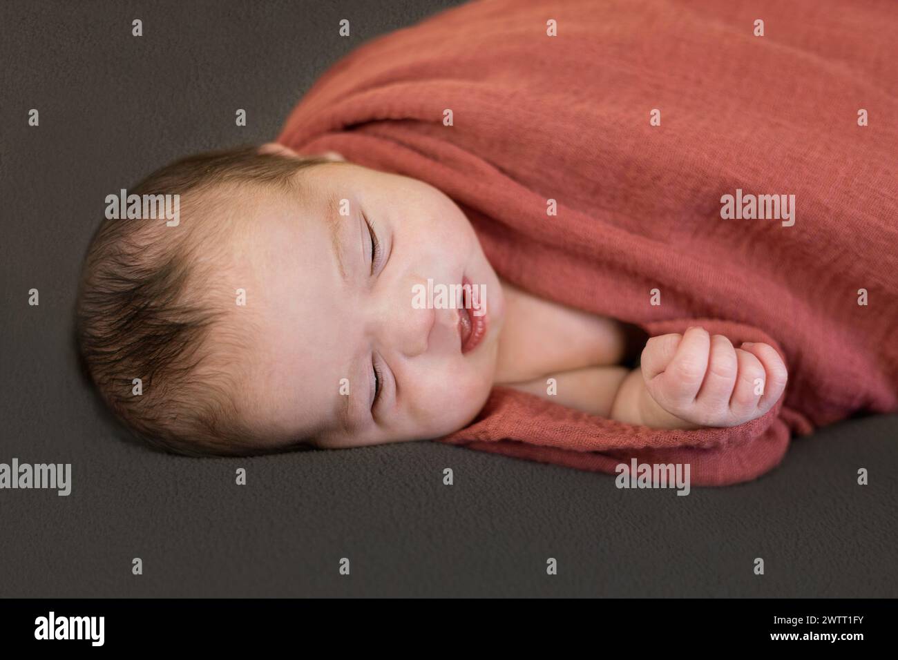 One week old newborn baby girl sleeping wrapped in cloth for studio ...