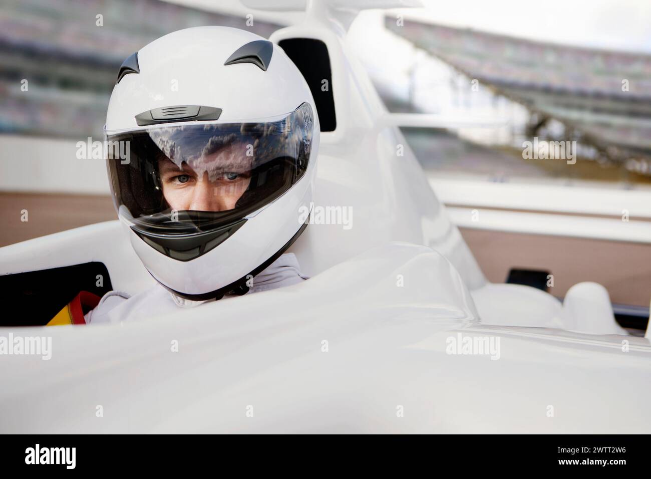 A focused individual clad in a white racing helmet sits in the cockpit ...