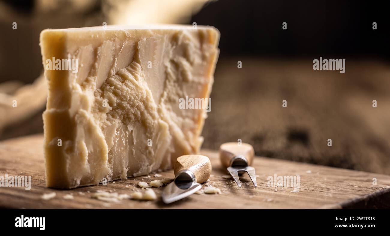 A block and pieces of Parmesan cheese on a cutting board along with a ...