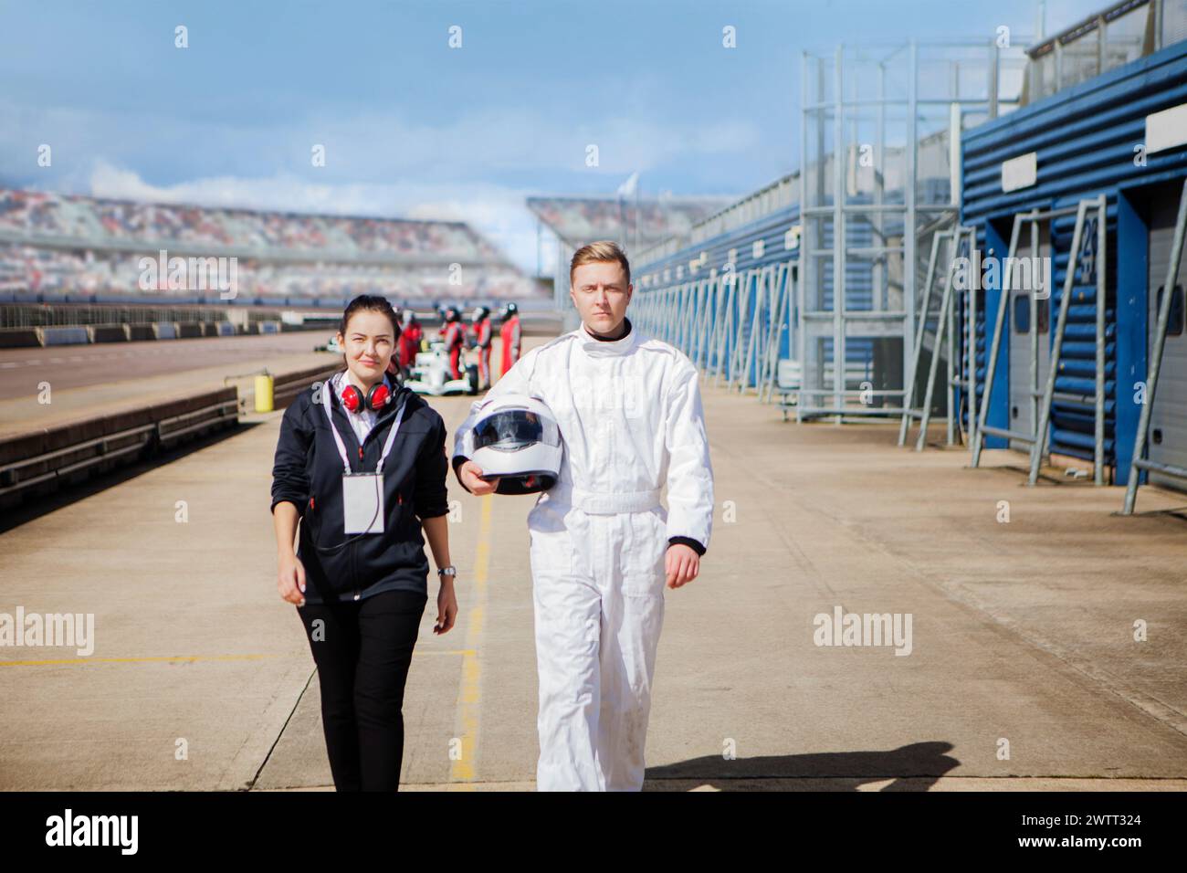 Confident race car driver walking with a technician at the racetrack ...