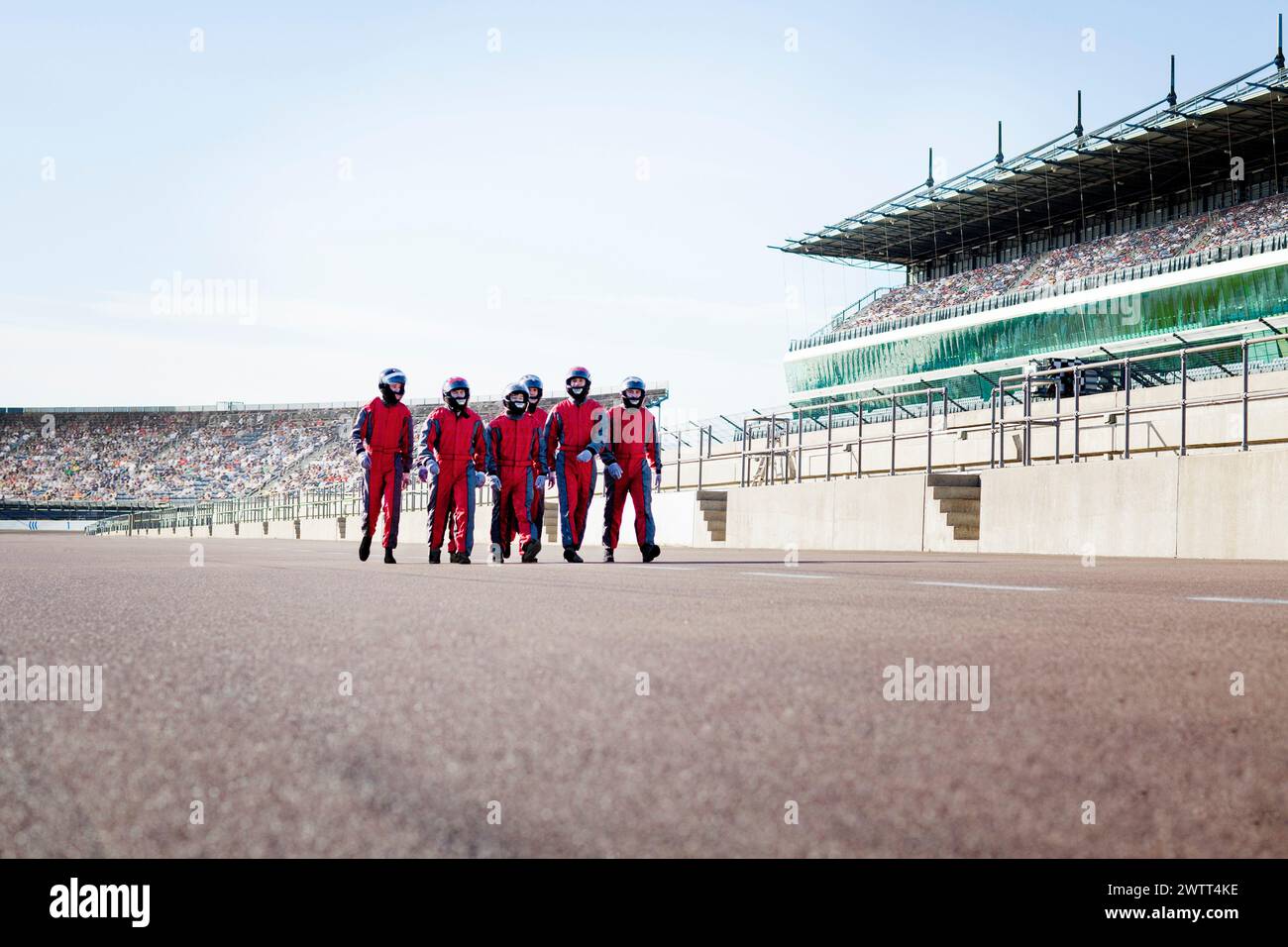 Pit crew team poised on racetrack with grandstand in the background ...