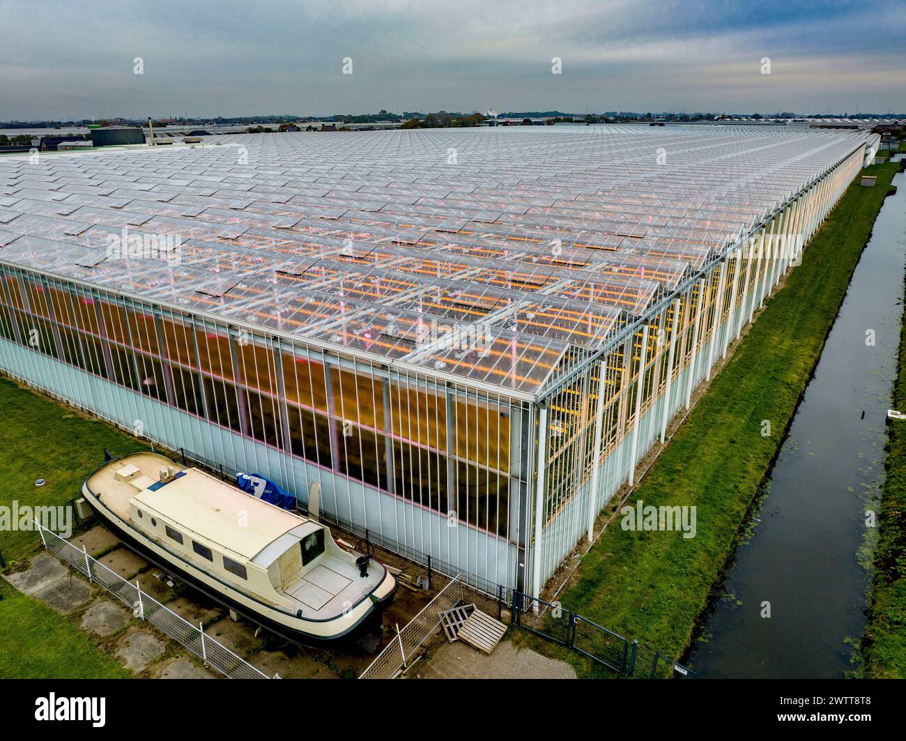 Aerial view of a vast greenhouse complex next to a canal with a white ...