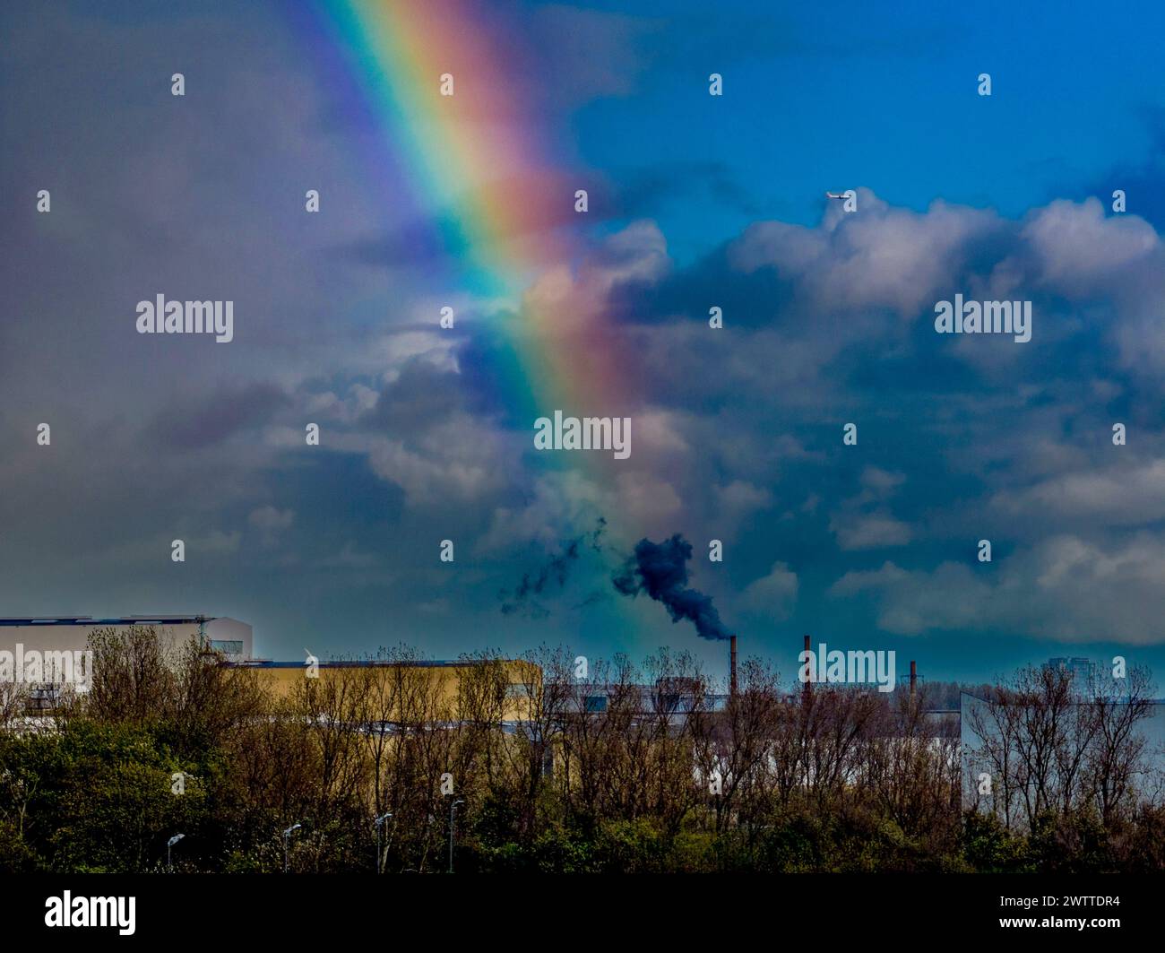 A dramatic rainbow cuts through a stormy sky above an industrial ...