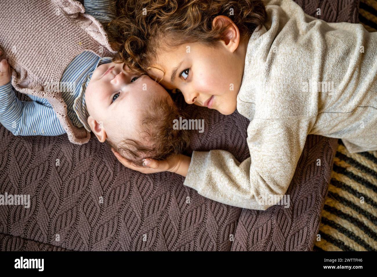 A tender moment as a young child lovingly gazes at a baby sibling ...