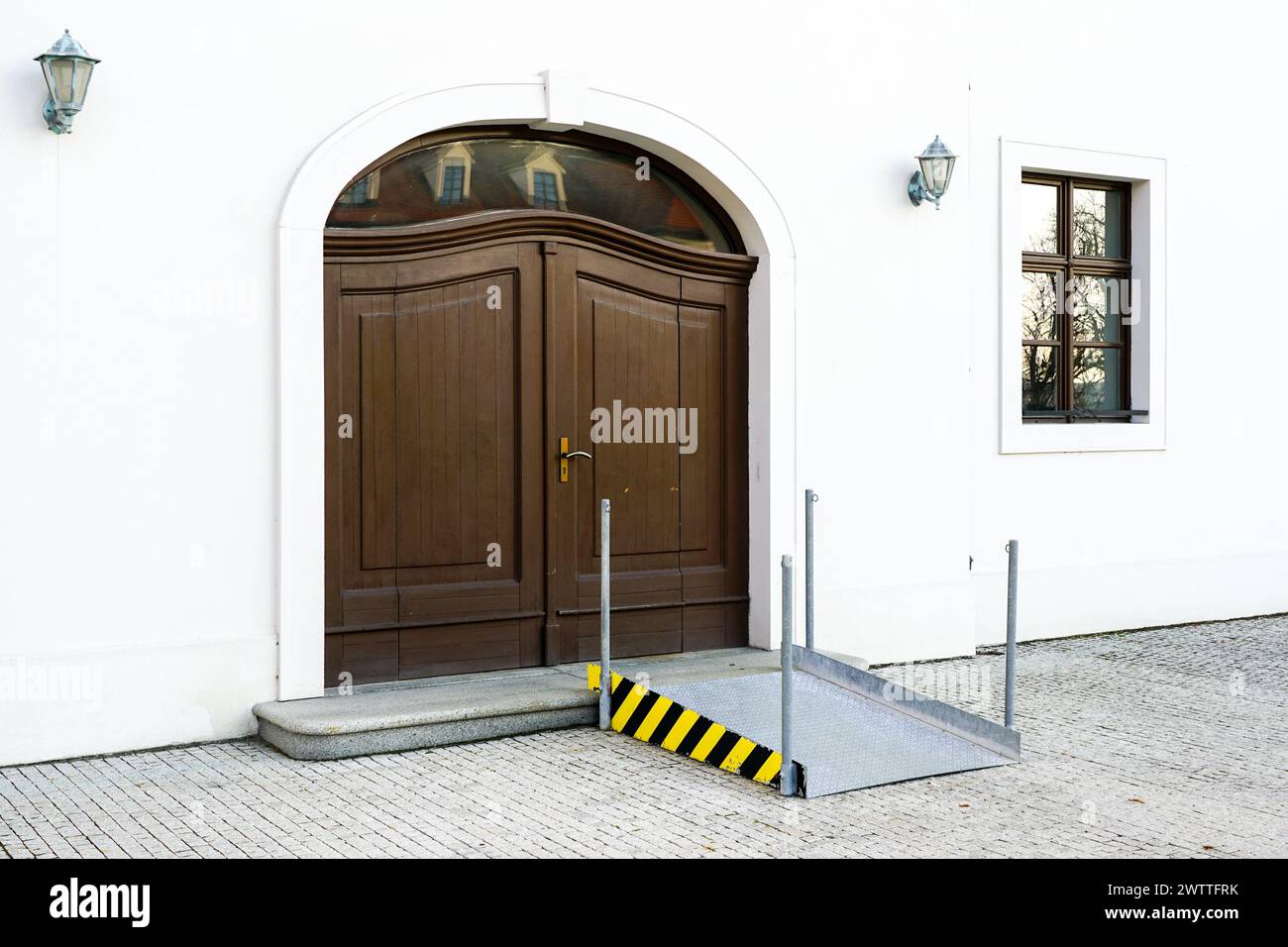 A compact metal wheelchair ramp at the entrance door of a public ...
