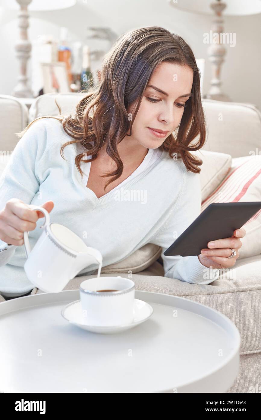 Woman pouring milk into coffee while reading a tablet Stock Photo - Alamy