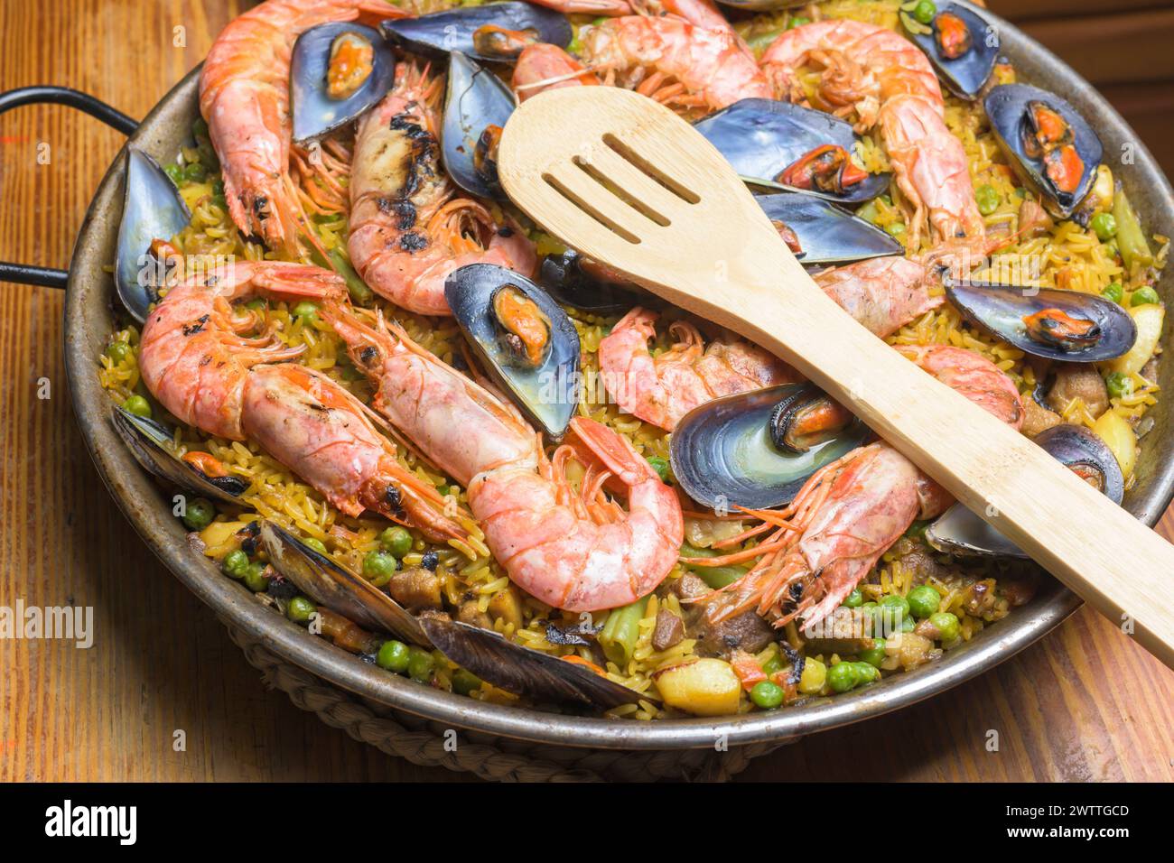 A paella full of seafood, peas, and rice served in a pan with a wooden ...