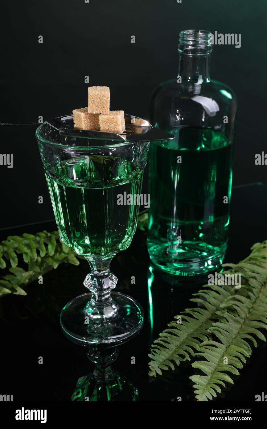 Absinthe, brown sugar, spoon and green leaves on mirror table ...