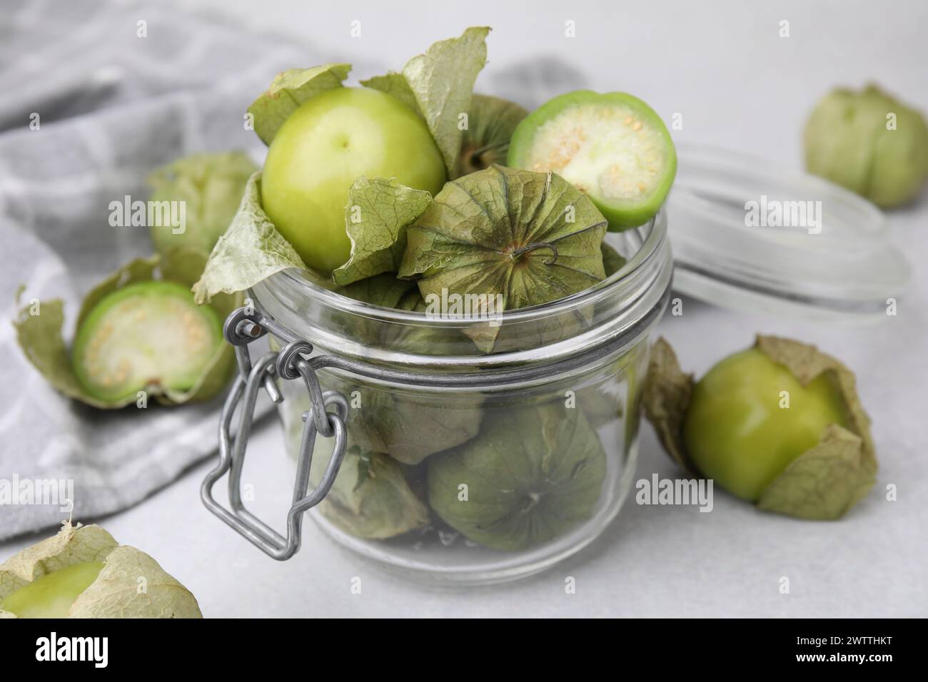 Fresh green tomatillos with husk in glass jar on light table, closeup ...