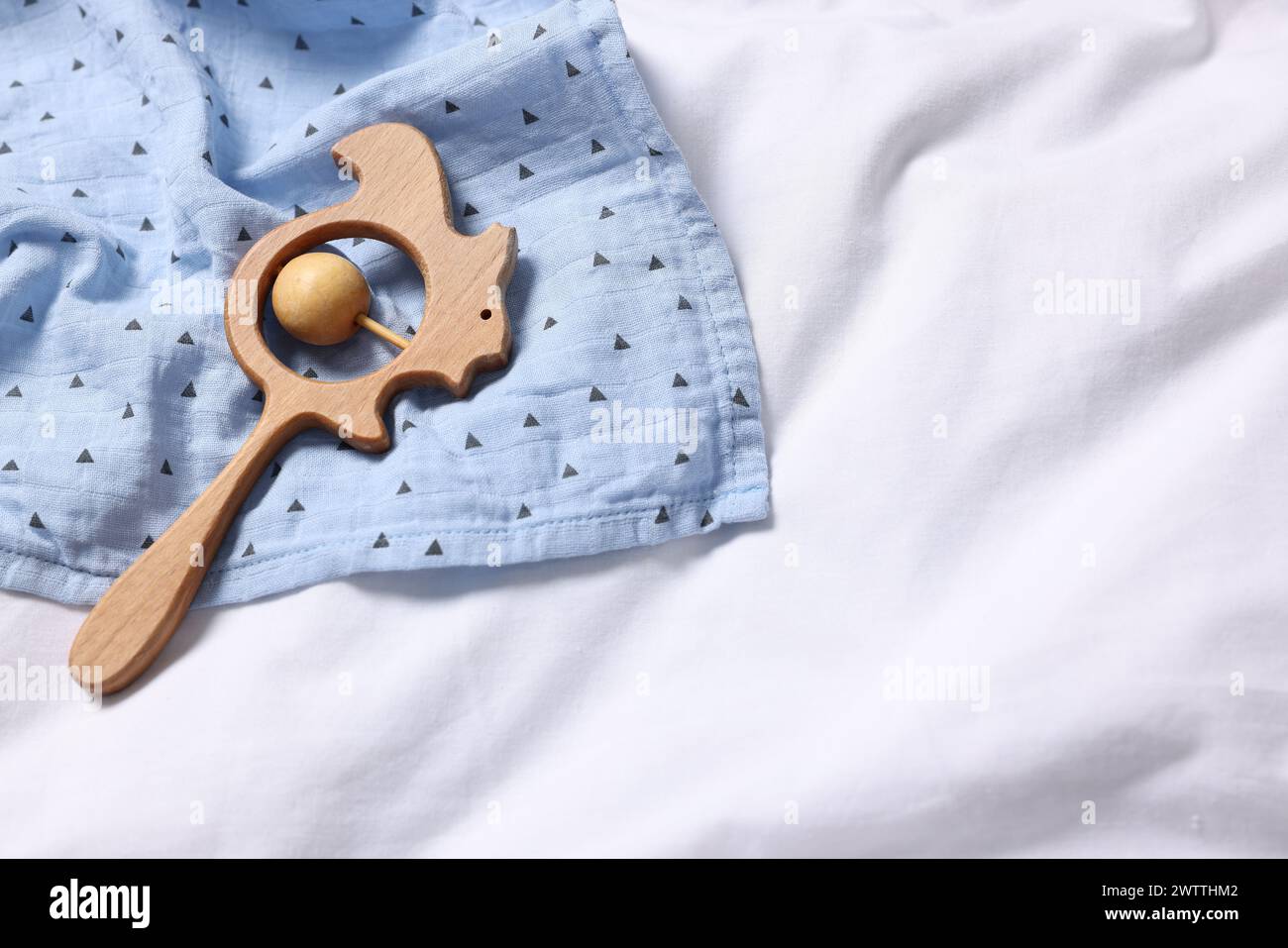 Baby accessories. Wooden rattle and cloth on white fabric, top view ...
