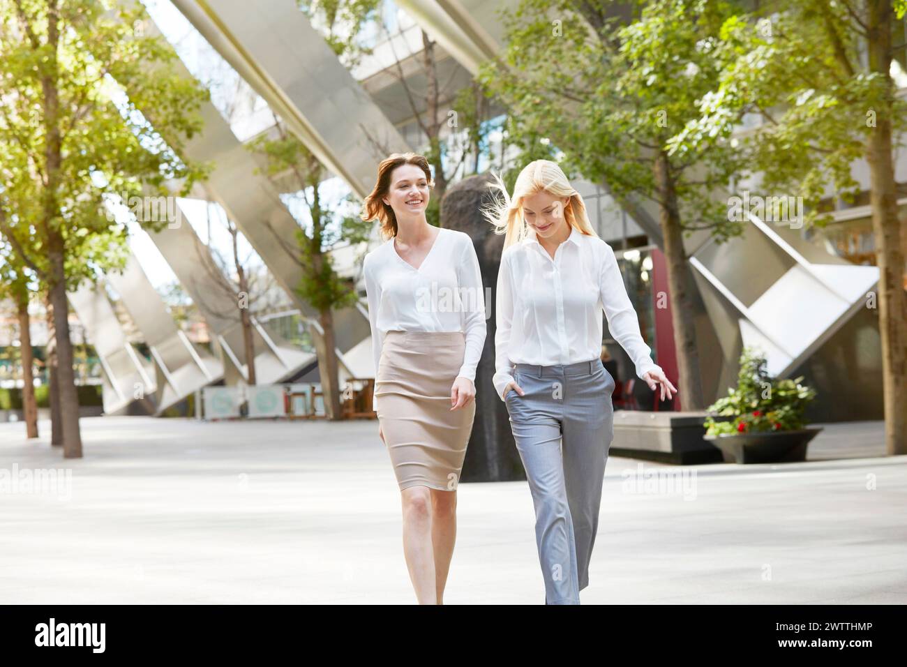 Two women walking and chatting in an urban plaza Stock Photo - Alamy