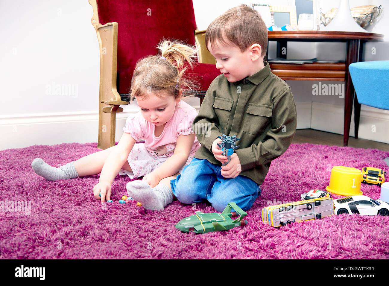 Two kids playing with toys on a purple carpet Stock Photo - Alamy