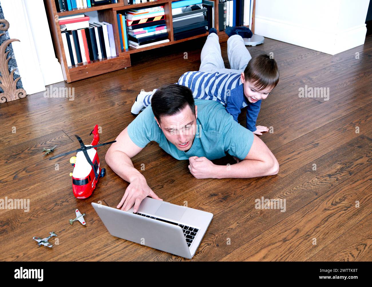 Man working on laptop with child playing behind him Stock Photo - Alamy