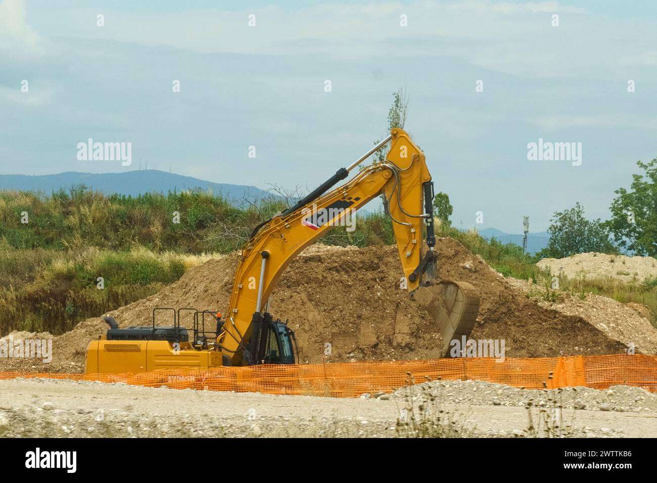 A large yellow excavator in action, digging into a pile of dirt at a ...