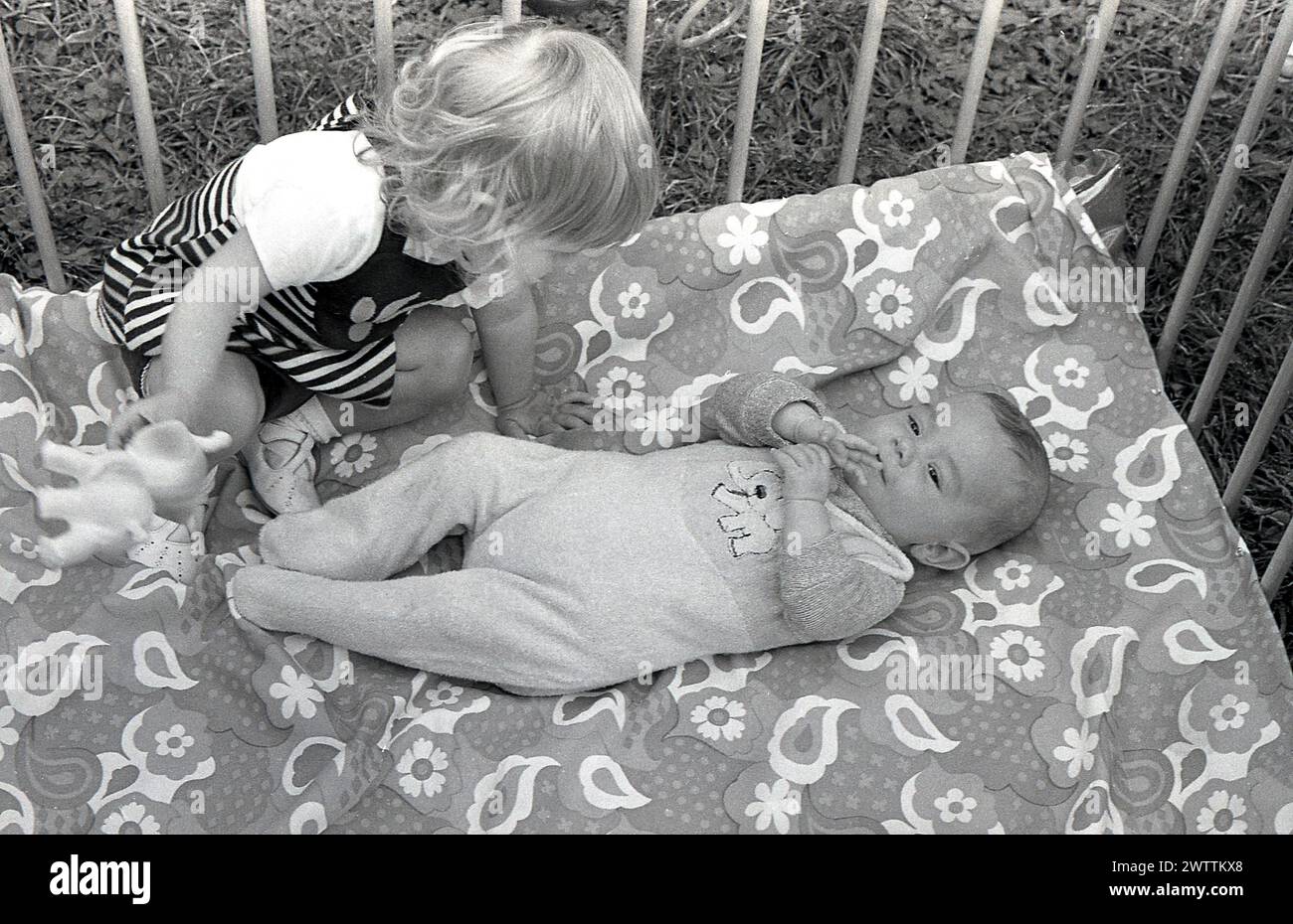 1970s, historical, a little girl with her infant brother lying in his a ...
