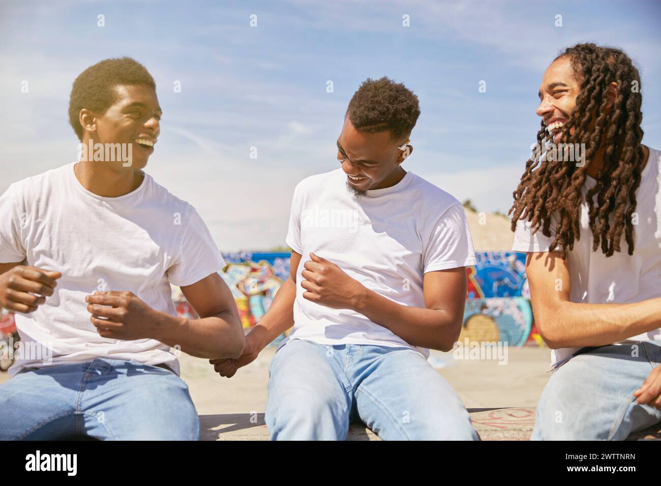 Three friends laughing and sitting together outdoors Stock Photo - Alamy