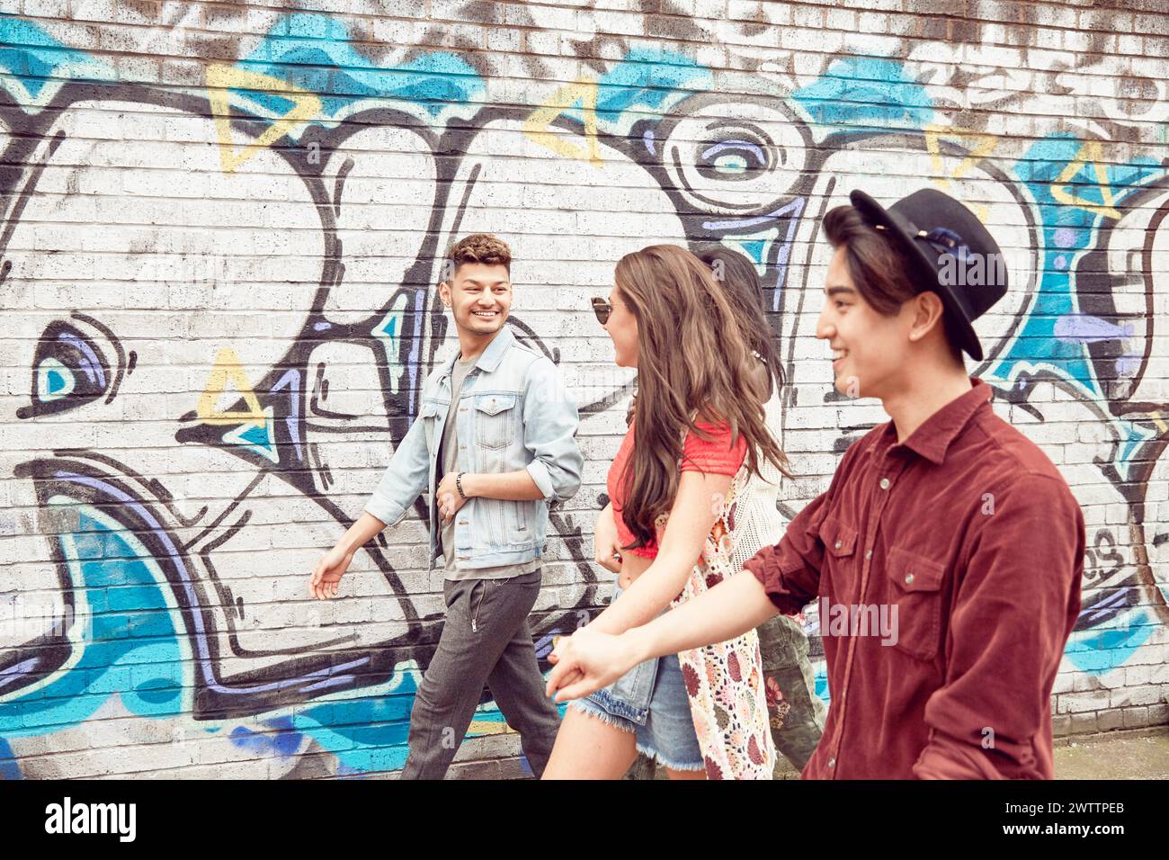 Three friends walking by a graffiti wall Stock Photo - Alamy