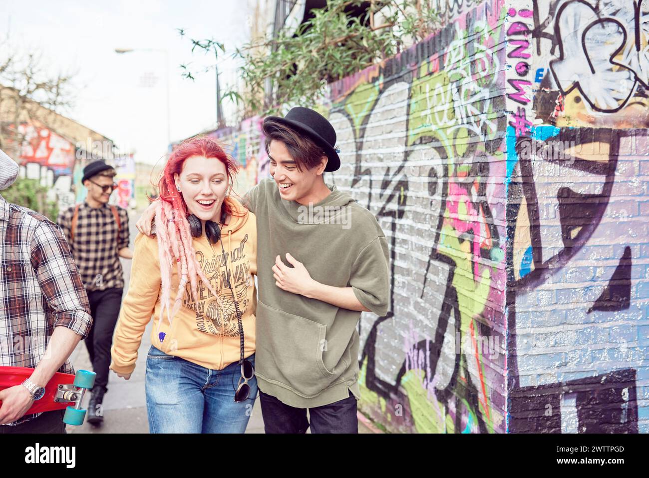Two friends laughing and walking by graffiti wall Stock Photo - Alamy
