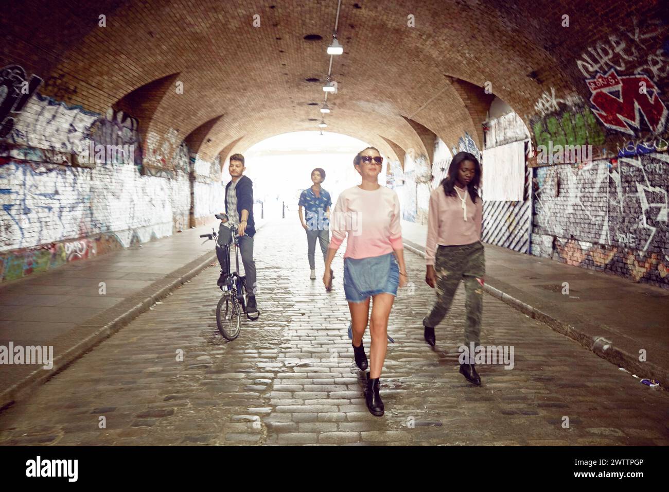 Group of friends walking under a graffiti-covered archway Stock Photo ...
