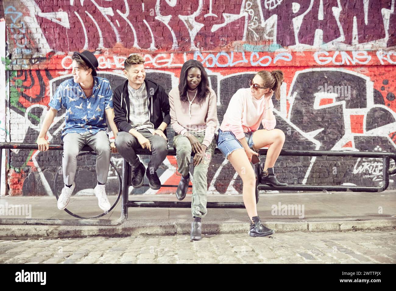 Friends sitting on a railing with graffiti background Stock Photo - Alamy
