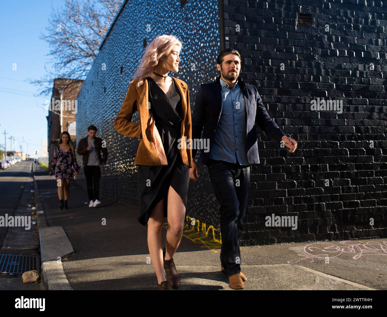 Couple walking on a city sidewalk with mural Stock Photo - Alamy